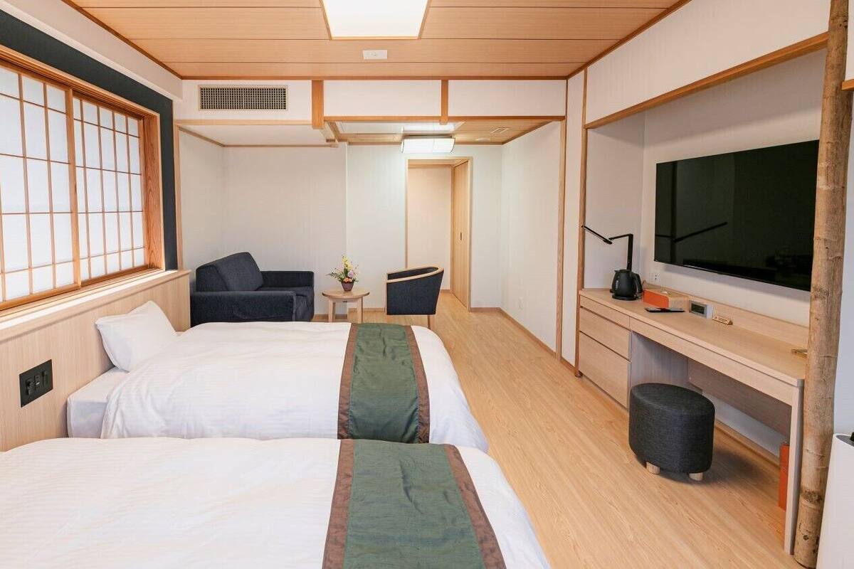 Quarto de hotel com duas camas, televisão, secretária e pequena mesa com abajur.