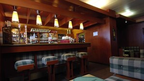 Zona de bar com banquetas de madeira, balcão com diversas garrafas e luminárias pendentes.