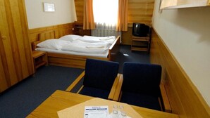 Quarto de hotel compacto com cama, uma pequena mesa com um menu, televisão e uma janela com cortinas.