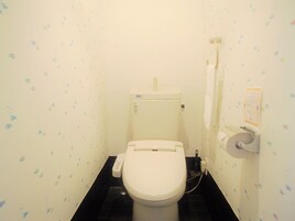 Casa de banho pequena e compacta, com sanita, dispensador de toalhas de papel e suporte de toalhas fixado na parede.