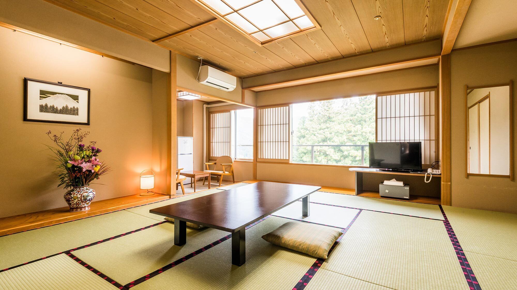 Um quarto japonês tradicional com tatames, uma mesa baixa, uma televisão e uma janela com vista para o verde.