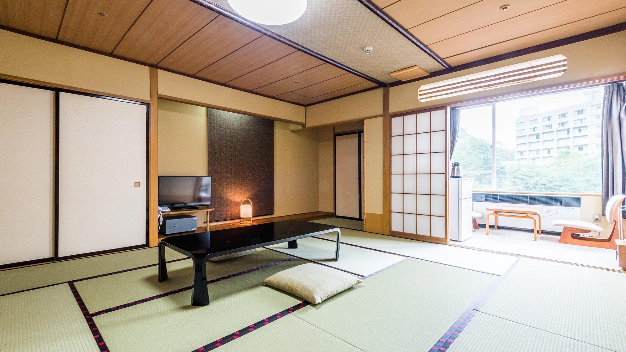 Um quarto japonês tradicional com tatames, uma televisão, um banco e portas de correr.