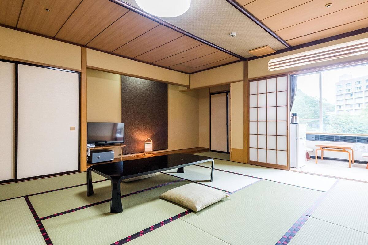 Um quarto japonês tradicional com tatames, uma mesa baixa, uma televisão e portas deslizantes.
