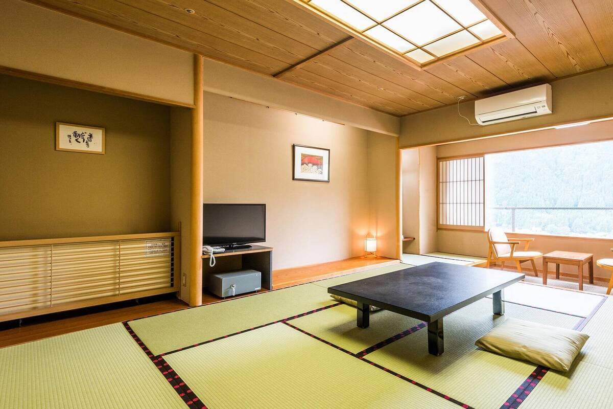 Quarto japonês tradicional com tatames, televisão, aquecedor, futon e vista para o exterior.