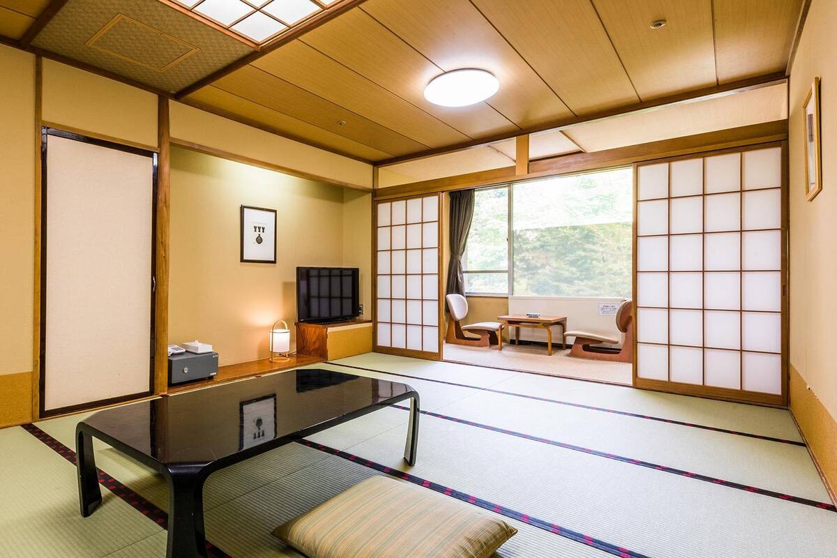 Um quarto japonês tradicional com tatames, uma mesa baixa, uma televisão e portas de correr.