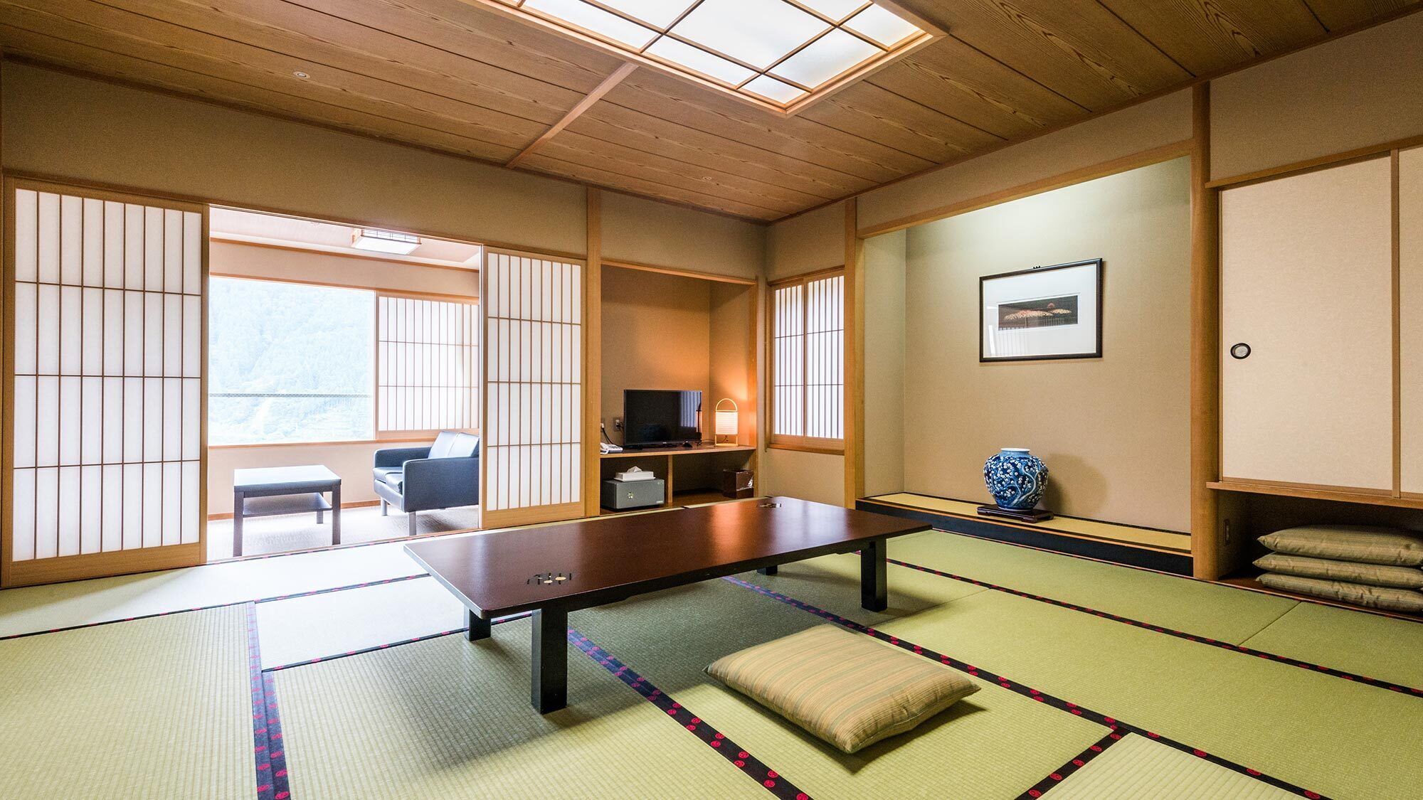 Um quarto japonês tradicional com tatames, uma mesa baixa, um sofá, uma televisão e um vaso.
