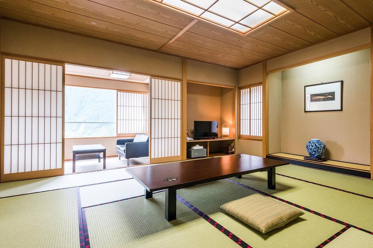 Um quarto japonês tradicional com tatames, uma mesa baixa, um sofá, uma televisão e um vaso.