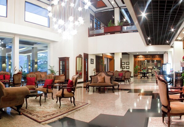 Um hall amplo com sofás de couro, um grande candelabro e vista para o restaurante ao fundo.