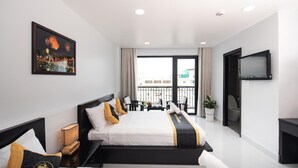 Quarto de hotel com uma cama grande, uma escrivaninha, uma cadeira, televisão e varanda com vista para edifícios.