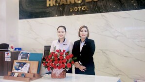 Bancada de recepção no Hotel Hoàng Long, com parede de mármore, placa de identificação e arranjo floral.