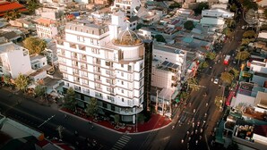 Vista aérea de um hotel com vários andares e uma estrutura de cúpula imponente, situado em um ambiente urbano denso com ruas estreitas e diversos edifícios.