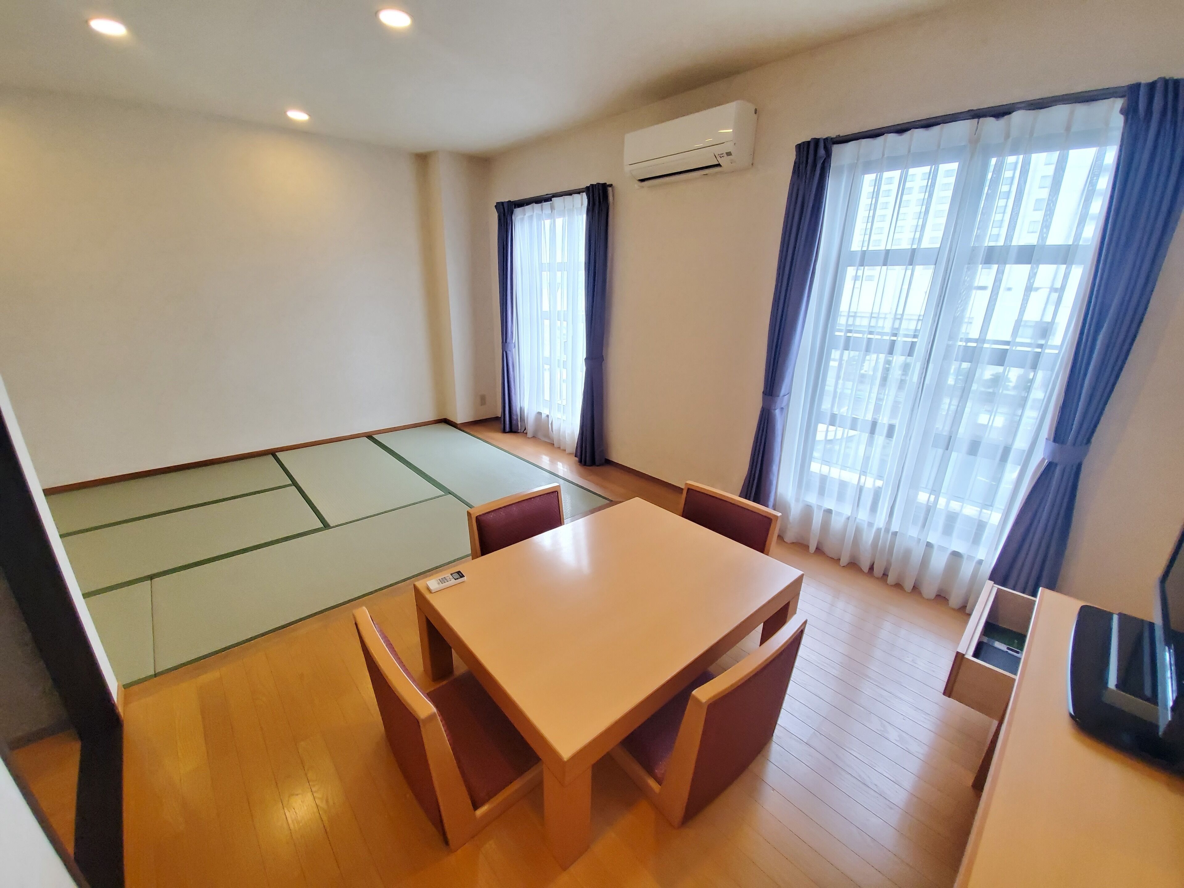Quarto com tatames, uma mesa de madeira com cadeiras, uma televisão e um ar condicionado.