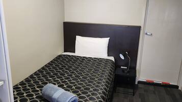Quarto de hotel com cama, mesa de cabeceira, abajur e porta.