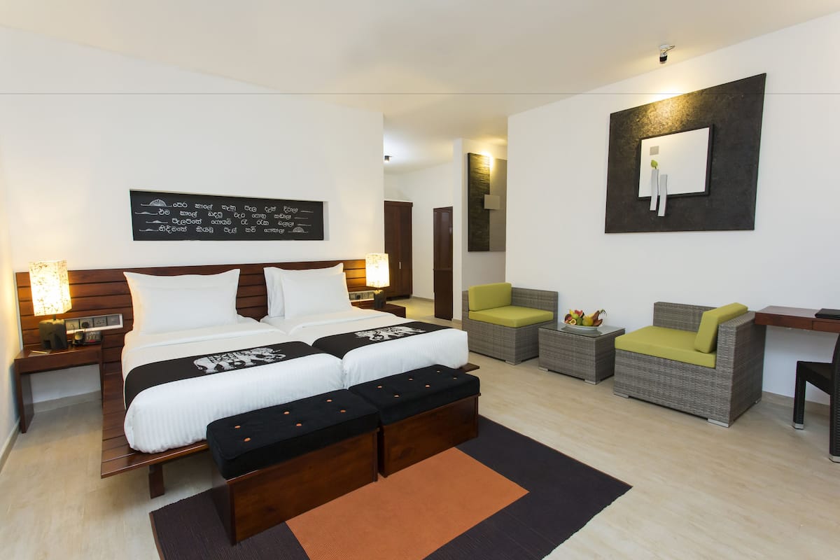 Quarto de hotel moderno com uma cama grande, uma escrivaninha, uma cadeira e uma mesa pequena com objetos decorativos.