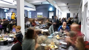 Restaurante lotado com mesas postas para refeições, uma grande escultura amarela e vista para o exterior.