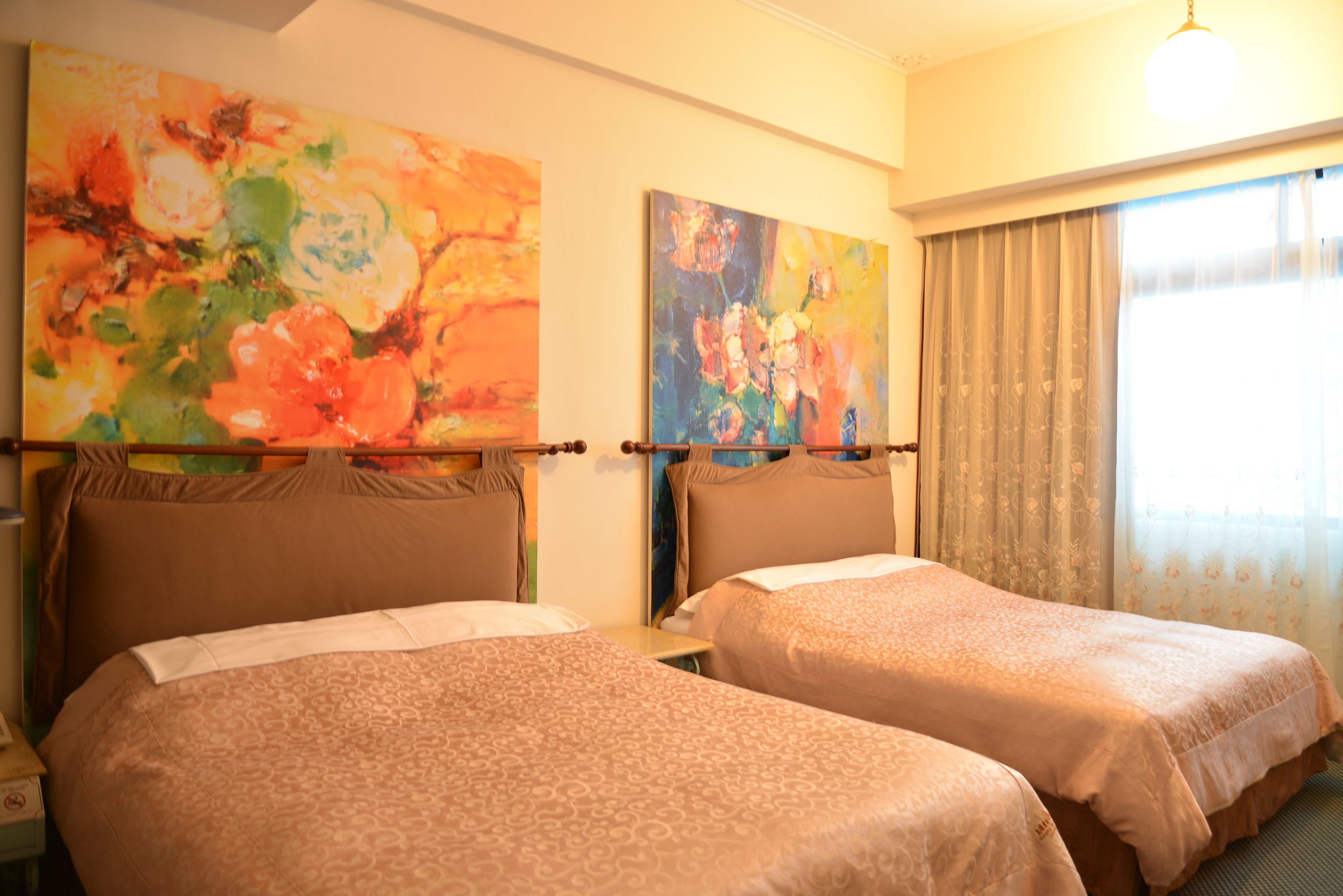 Quarto de hotel com duas camas, uma pintura abstrata grande na parede e uma janela com cortinas.