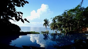 Visão nítida de uma piscina com o reflexo de palmeiras e do oceano.