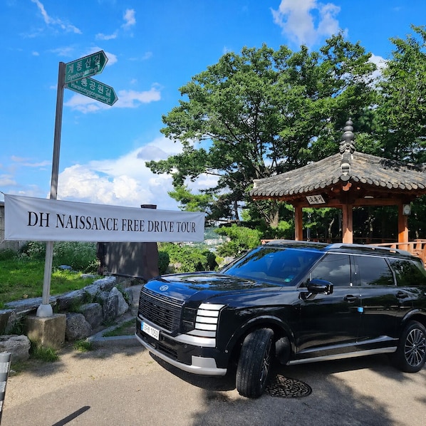 Um SUV preto estacionado em frente a uma placa que diz 'DH NAISSANCE FREE DRIVE TOUR'.