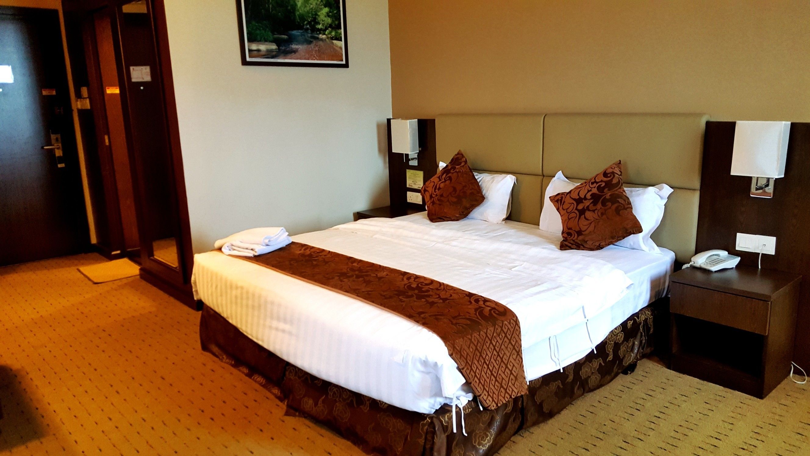 Quarto de hotel com uma cama grande, mesa de cabeceira com telefone e uma porta à esquerda.