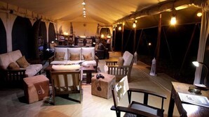 Acomodação em tenda com interior acolhedor, incluindo sofás, uma mesa de jantar e uma pequena cozinha.