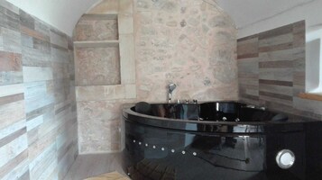 Uma casa de banho com uma banheira preta, paredes de pedra e uma janela.
