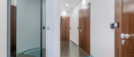Um corredor com portas de madeira, divisória de vidro e chão de azulejos.