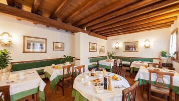 Um restaurante com vigas de madeira, bancos acolchoados verdes e mesas preparadas para o café da manhã.
