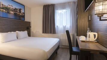 Quarto de hotel com cama, escrivaninha com chaleira, cadeira, janela com cortinas e um quadro na parede.