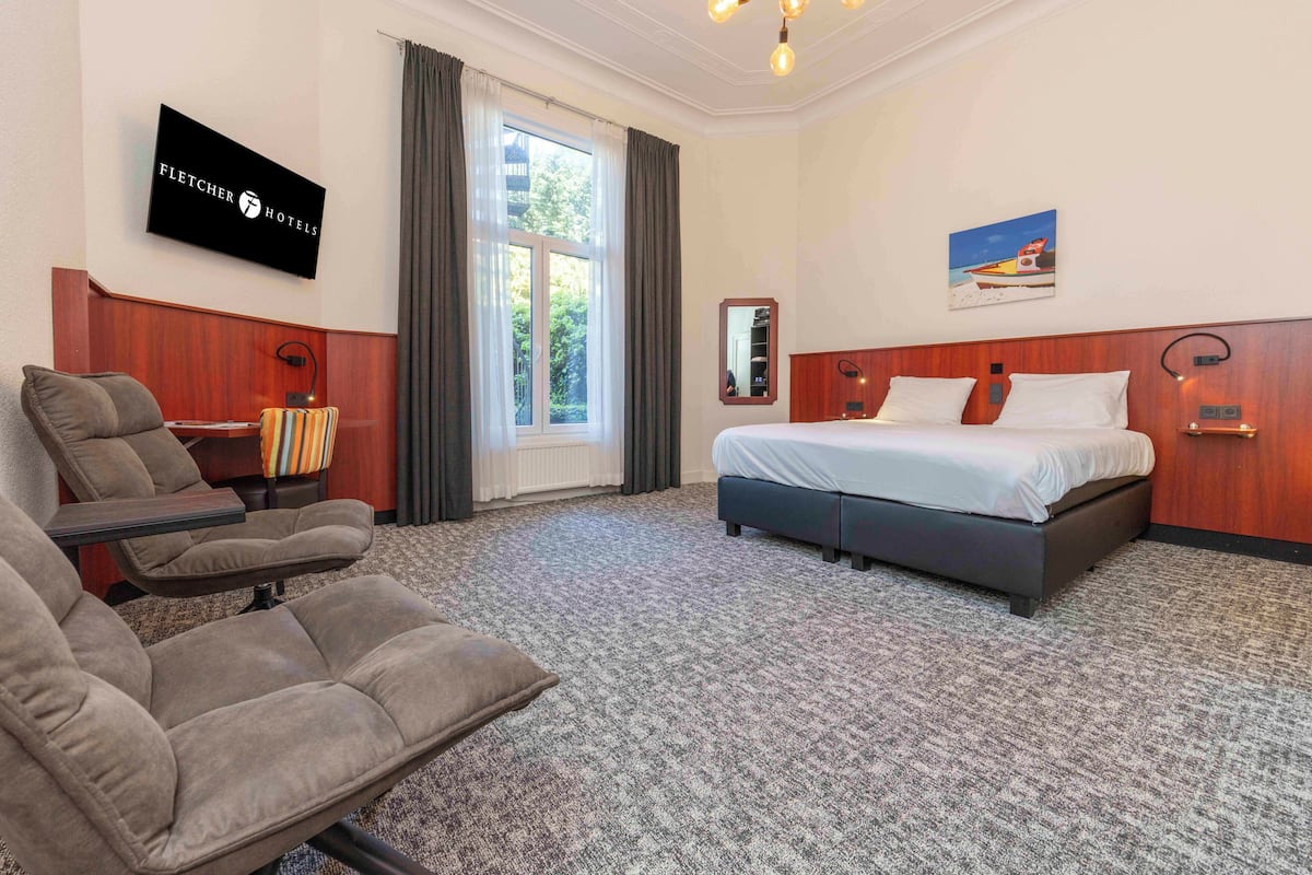 Quarto de hotel com cama, poltrona, televisão, janela e um quadro.
