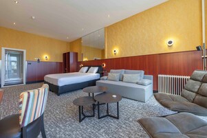 Quarto de hotel com cama, sofá, poltrona, duas mesinhas e espelho.