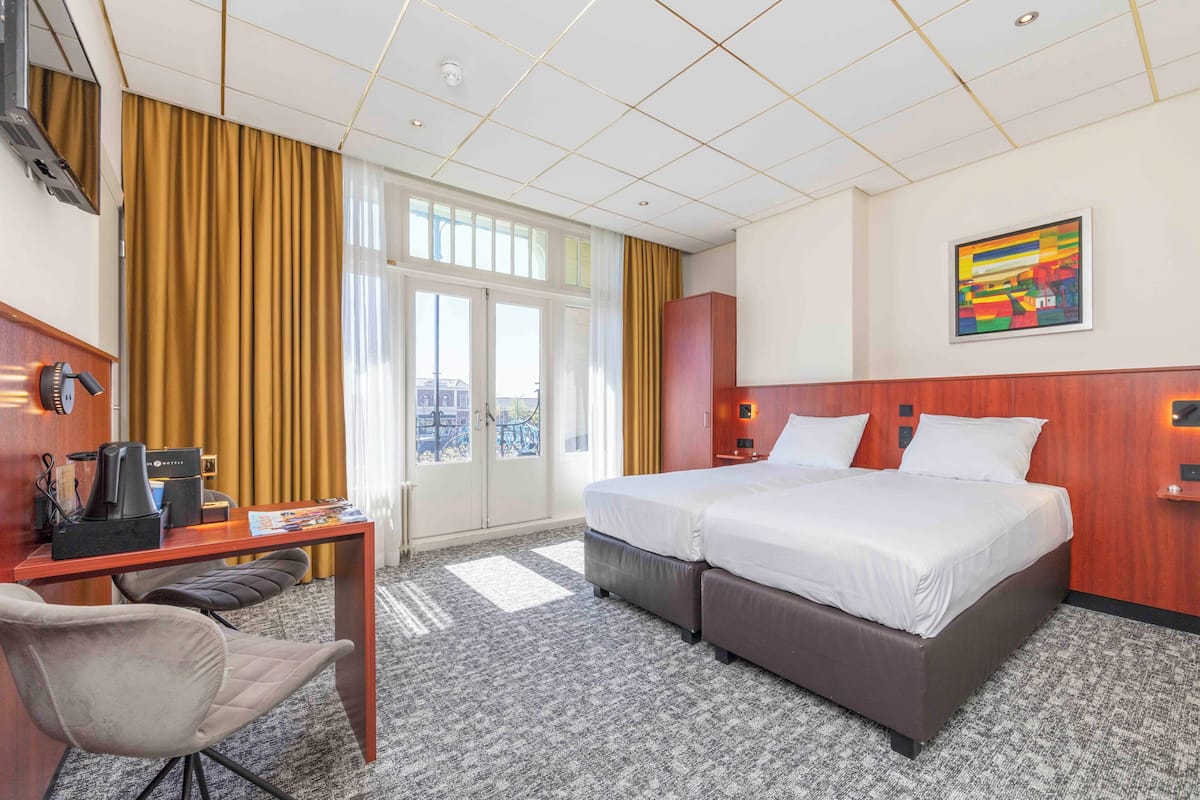 Quarto de hotel com cama, escrivaninha, cadeira e um quadro na parede.