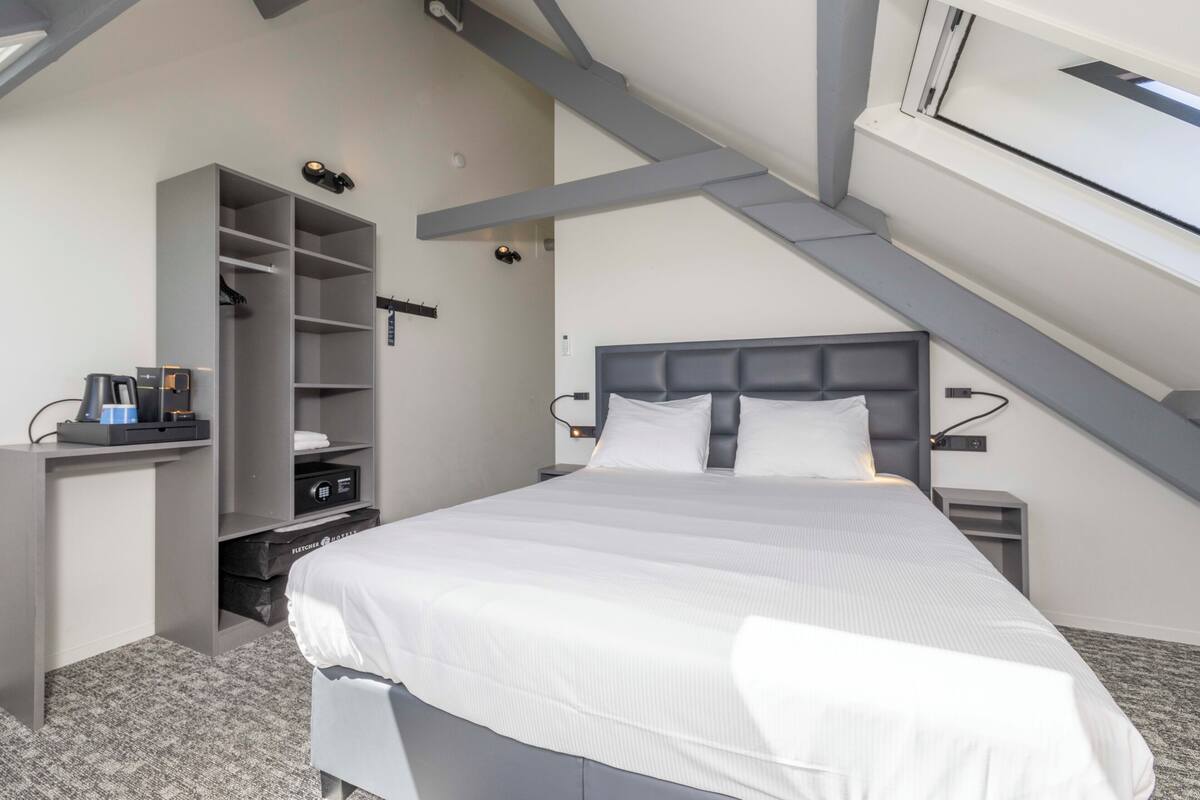 Quarto de hotel moderno com cama, escrivaninha embutida, guarda-roupa e teto inclinado.