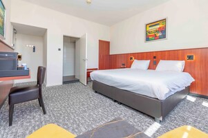 Quarto de hotel com cama, escrivaninha, cadeira e um quadro na parede.