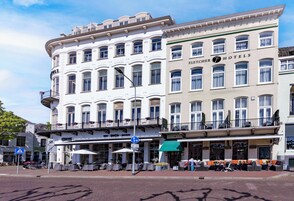 Um hotel de vários andares com estilo arquitetônico europeu clássico, com varandas adornadas com floreiras, áreas de estar ao ar livre e uma placa de hotel bem visível.