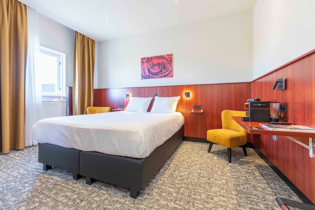 Quarto de hotel com cama, escrivaninha com computador, cadeira e televisão na parede.