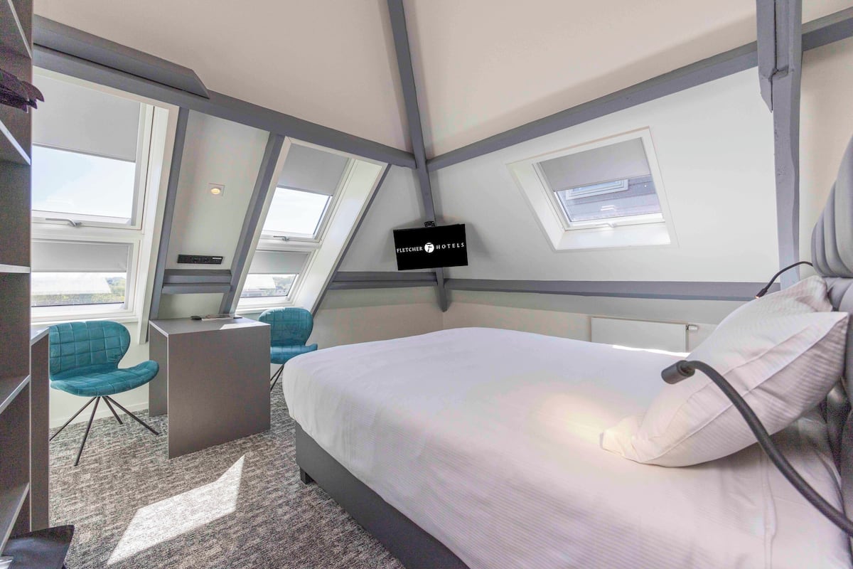 Quarto de hotel moderno com uma cama, uma escrivaninha, uma cadeira e uma televisão.