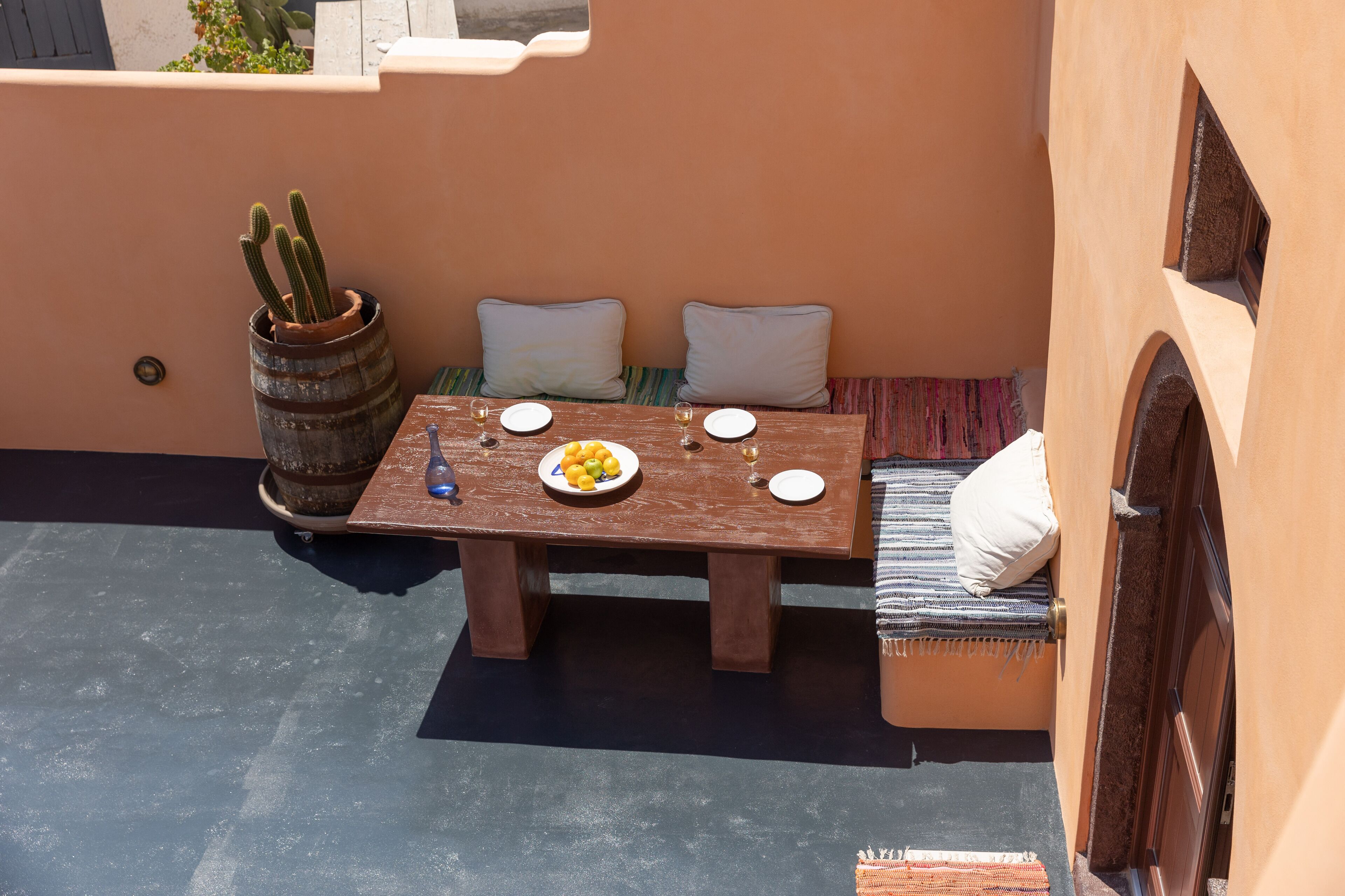 Uma mesa de madeira com pratos e um vaso de cacto, em frente a uma parede cor de pêssego com uma janela.
