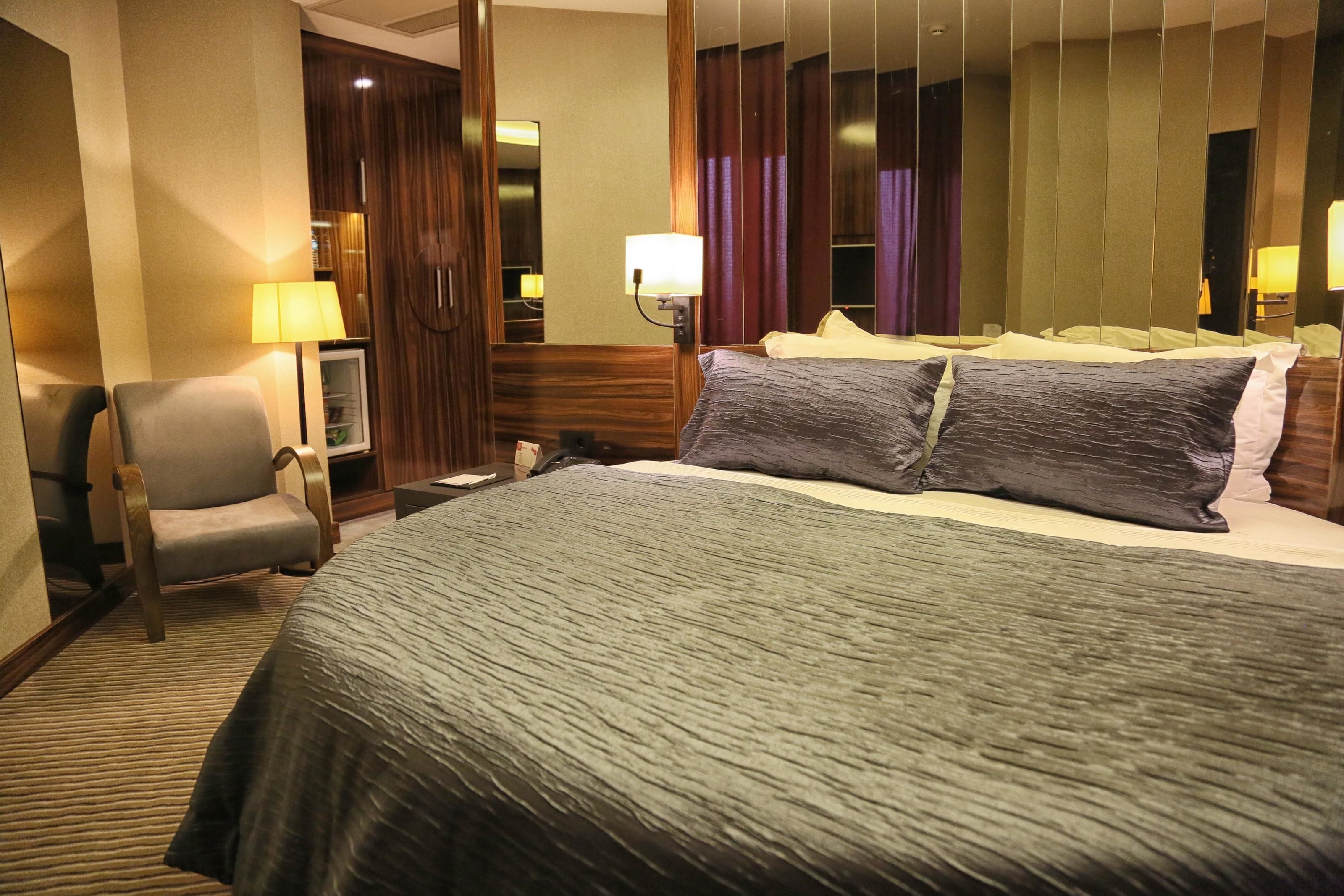 Quarto de hotel com uma cama grande, uma cadeira, uma escrivaninha e um espelho.