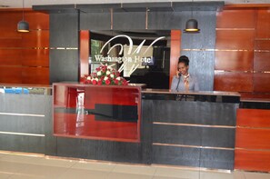 Bancada de recepção do Hotel Washington, com design moderno, divisória de vidro e um arranjo floral.