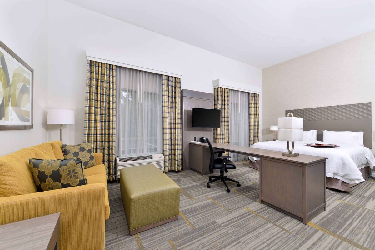 Quarto de hotel com cama, escrivaninha, cadeira, televisão e sofá.