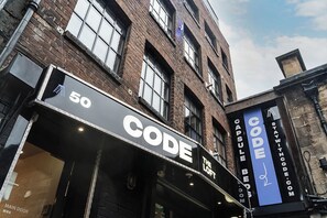 Um edifício com uma placa que diz 'CODE THE LOFT' e 'CAPSULE BEDROOMS', indicando um estabelecimento de hospedagem.