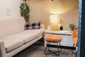 Uma sala de estar aconchegante com sofá, mesinha de centro, uma cadeira e uma planta decorativa.