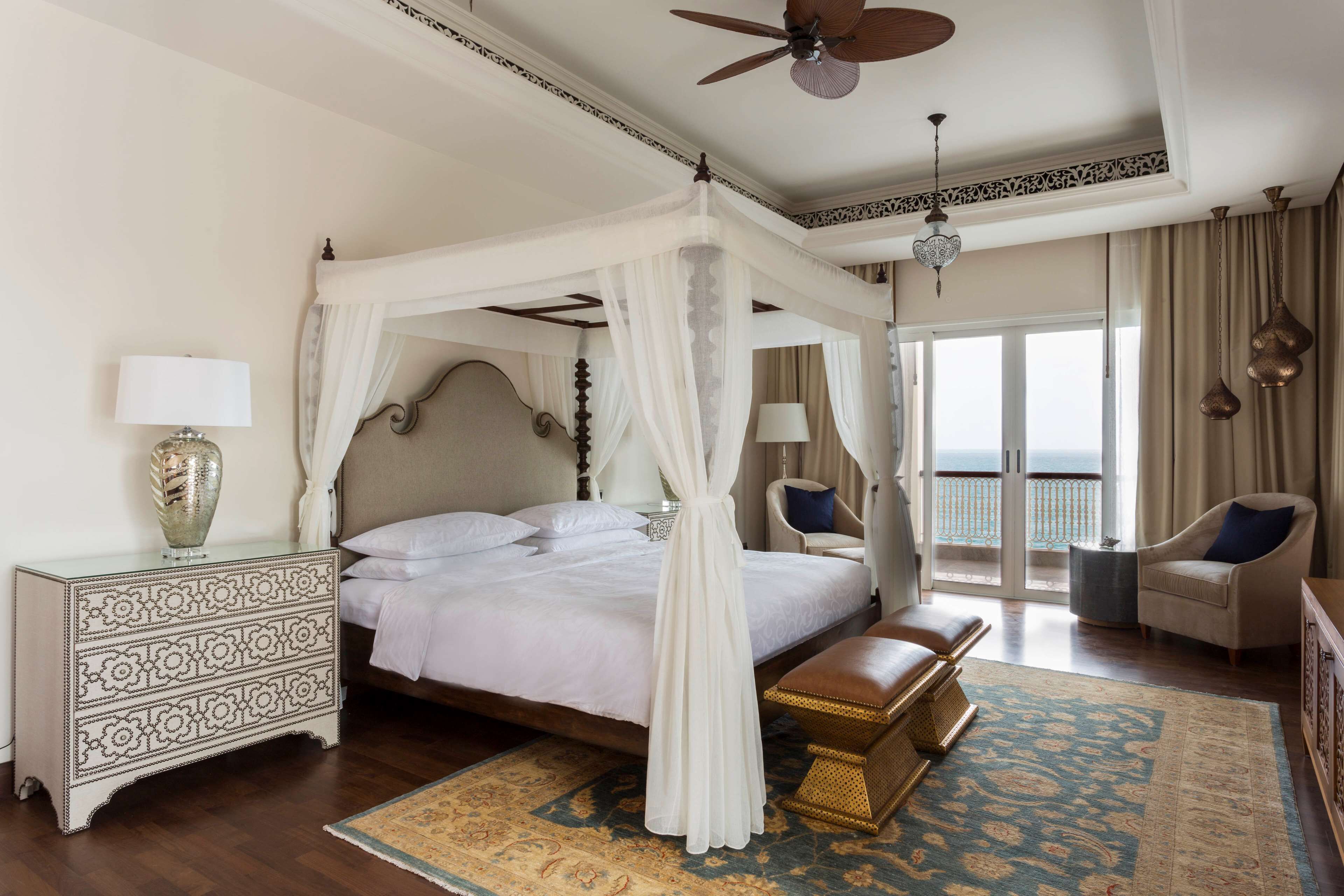 Um quarto espaçoso com cama de dossel, um espaço de estar com um banco e vista para o mar através de grandes janelas.