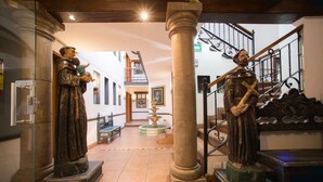 Um corredor com estátuas, escadaria e uma fonte.