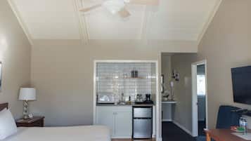 Quarto de hotel com cama, escrivaninha, cozinha compacta e ventoinha no teto.
