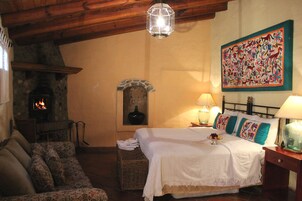 Um quarto aconchegante com lareira de pedra, cama com almofadas decorativas, cesta de vime e um quadro abstrato grande na parede.