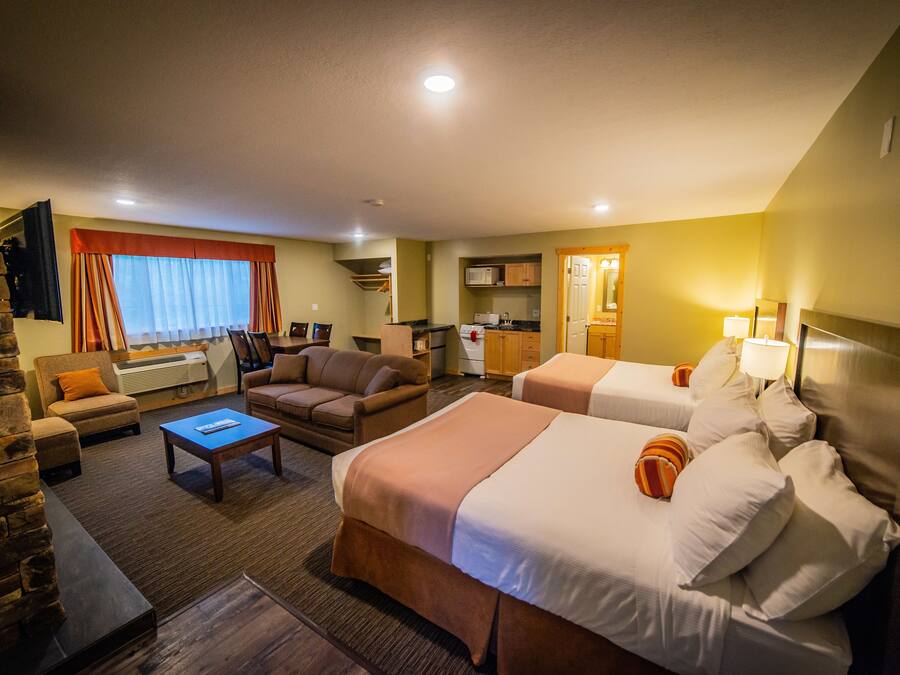 Quarto de hotel com duas camas, um sofá, uma mesa de centro e uma cozinha.
