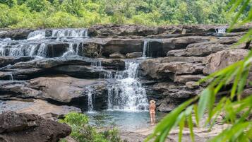 Uma cachoeira se derramando sobre terreno rochoso, com uma pessoa de pé na água.