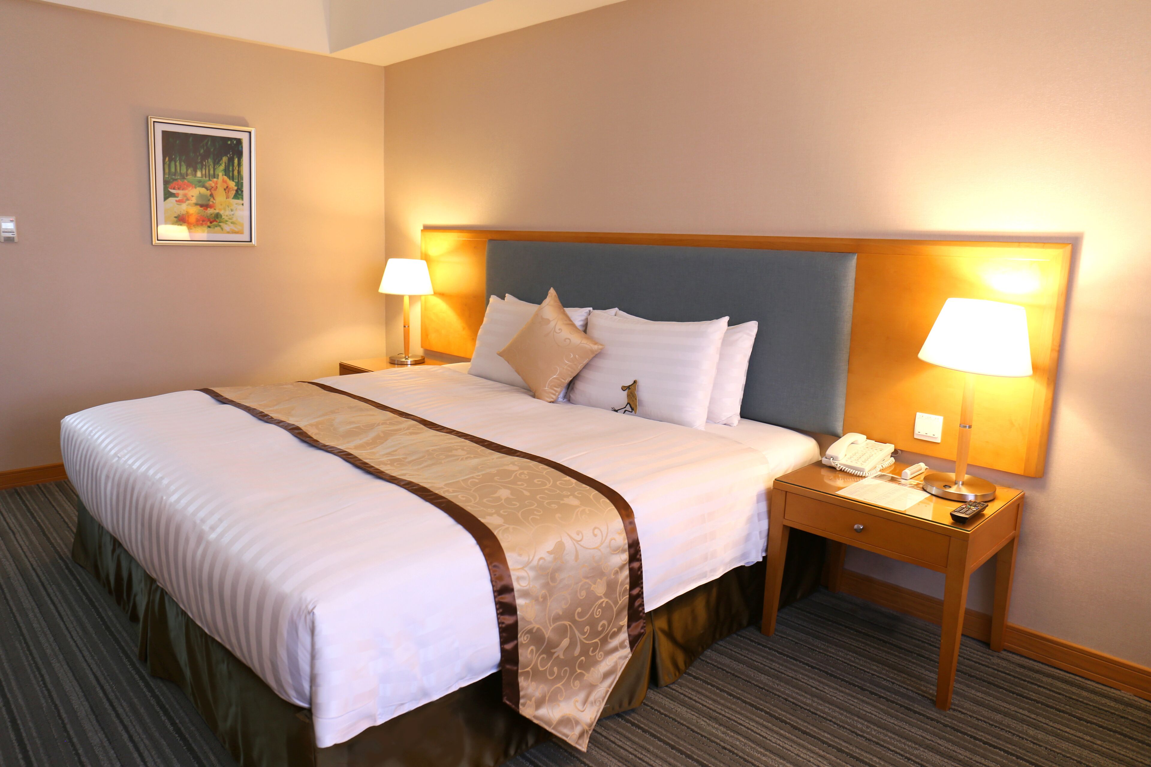 Quarto de hotel com uma cama grande, duas mesas de cabeceira, uma luminária e um quadro na parede.