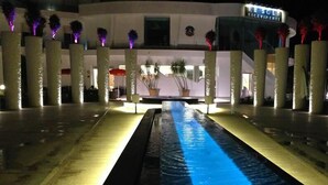 Um saguão de hotel com um elemento central de água, plantas em vasos e uma área de recepção.